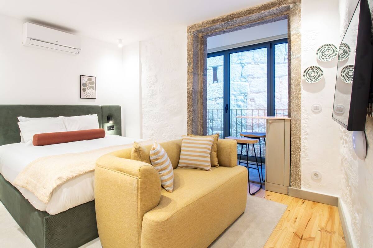 Quarto moderno com cama, sofá, mesinha e varanda com vista.