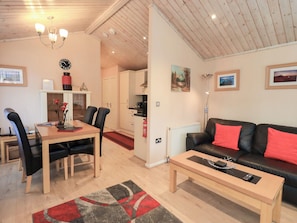 Uma sala de estar moderna com um sofá de couro preto, uma mesa de centro de madeira e uma área de jantar com mesa e cadeiras de madeira.