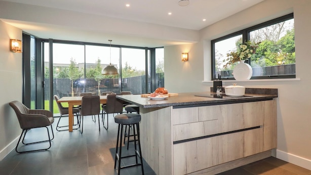 Uma cozinha moderna com uma ilha grande, banquetas e um espaço de refeições com mesa e cadeiras.