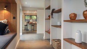 Interior moderno com área de cozinha, prateleiras de madeira e espaço de estar com um banco.
