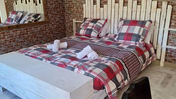Quarto com parede de tijolos, cabeceira de madeira, cama com colcha xadrez e mesa de cabeceira.