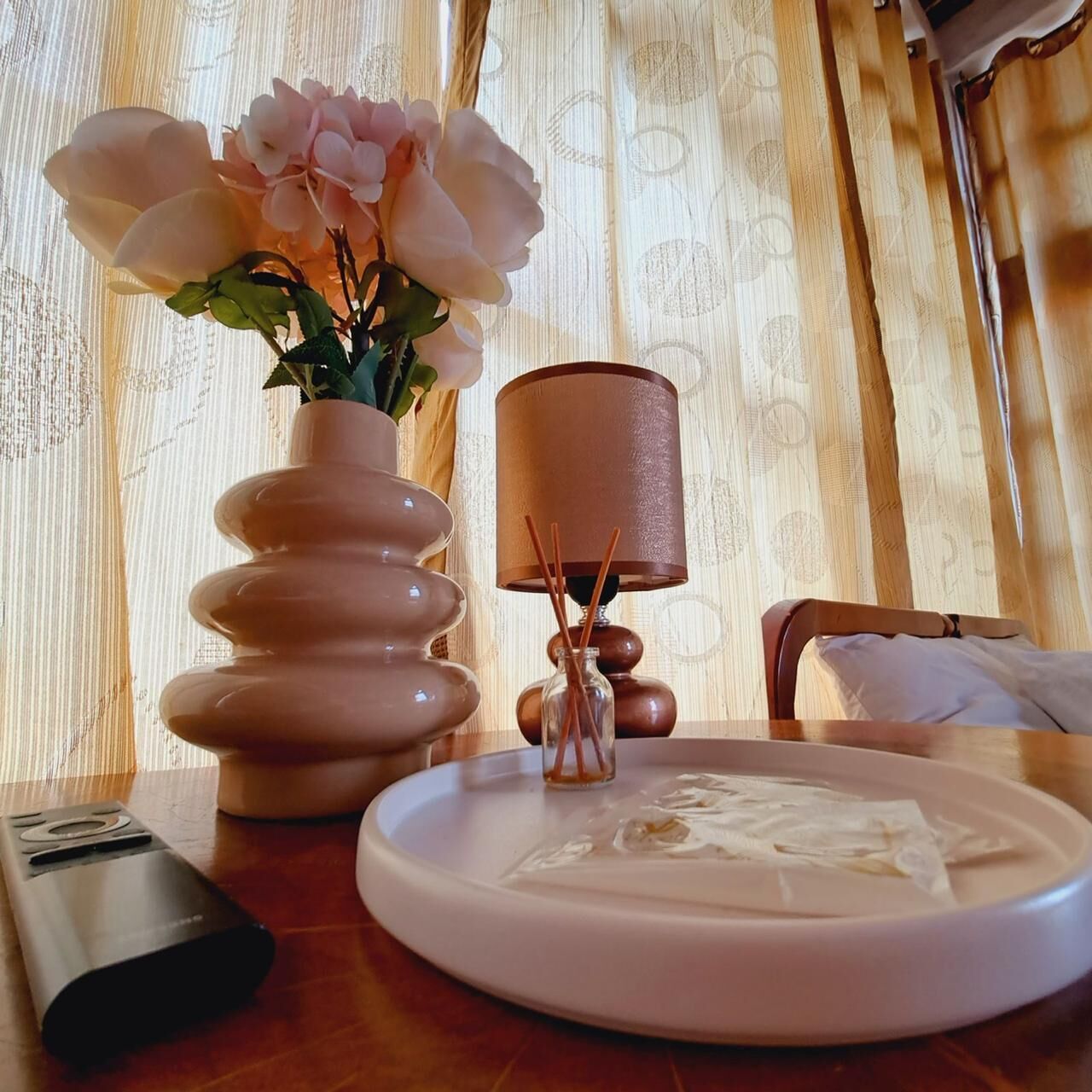 Uma mesa com um vaso de flores, uma lâmpada e um controle remoto.