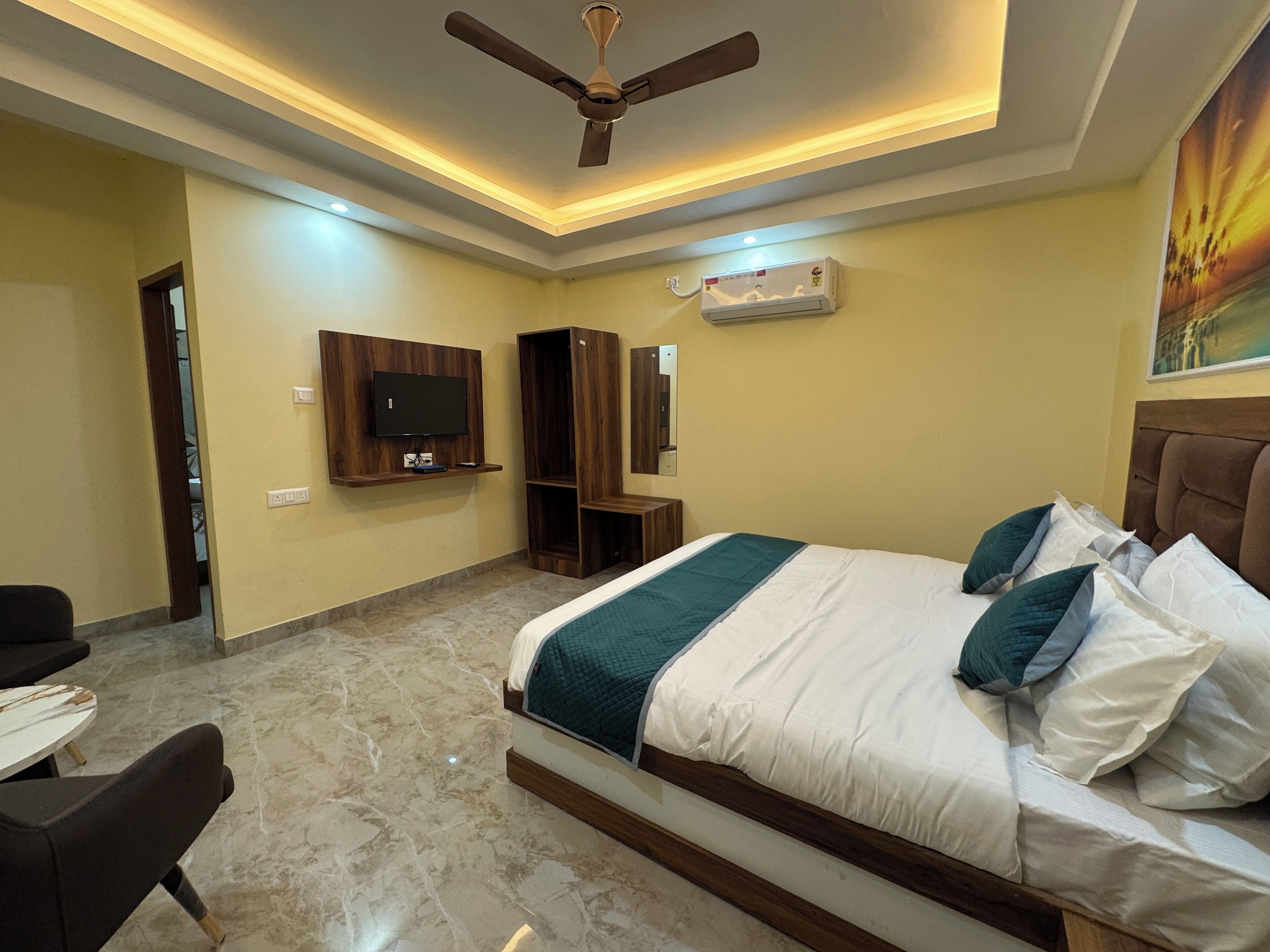 Quarto de hotel com cama, televisão presa à parede, ventoinha no teto e ar condicionado.