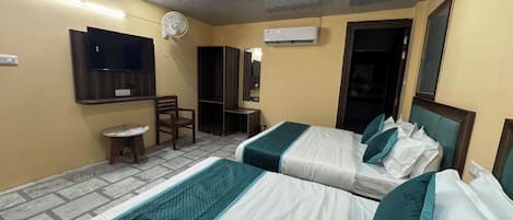 Quarto de hotel com duas camas, uma escrivaninha, uma cadeira, televisão e aparelho de ar condicionado.