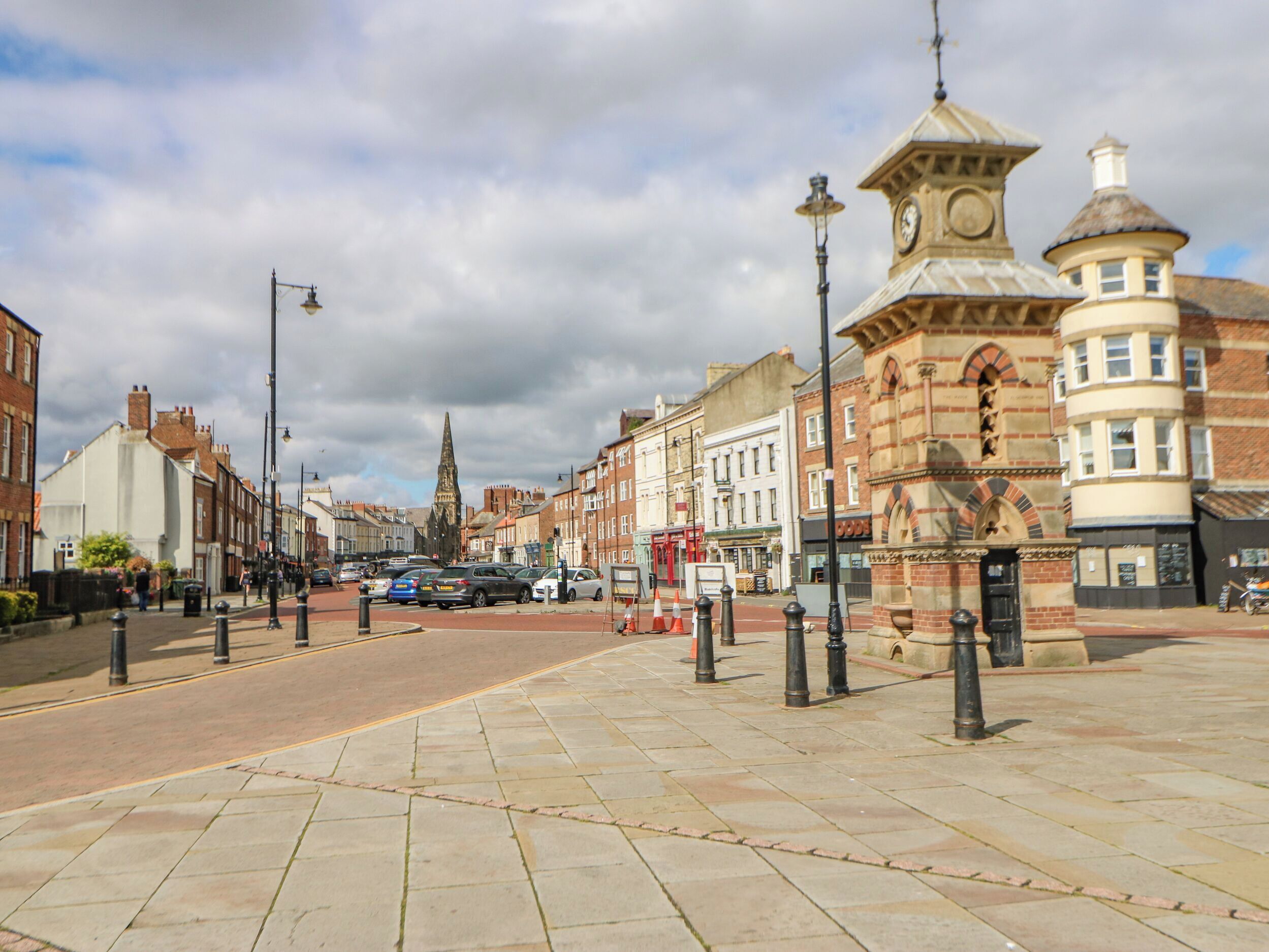 Uma praça histórica na cidade, com calçamento de pedras, arquitetura tradicional e uma torre do relógio imponente.