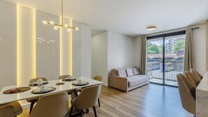 Uma zona de refeições moderna com uma mesa branca posta para quatro pessoas, um sofá e uma varanda com vista para edifícios.