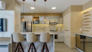 Uma cozinha moderna com ilha central, eletrodomésticos de aço inoxidável, iluminação pendente e uma parede de destaque em madeira.