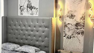 Um quarto moderno com cabeceira estofada, sofá cinzento, mesa redonda pequena e uma grande pintura abstrata na parede.