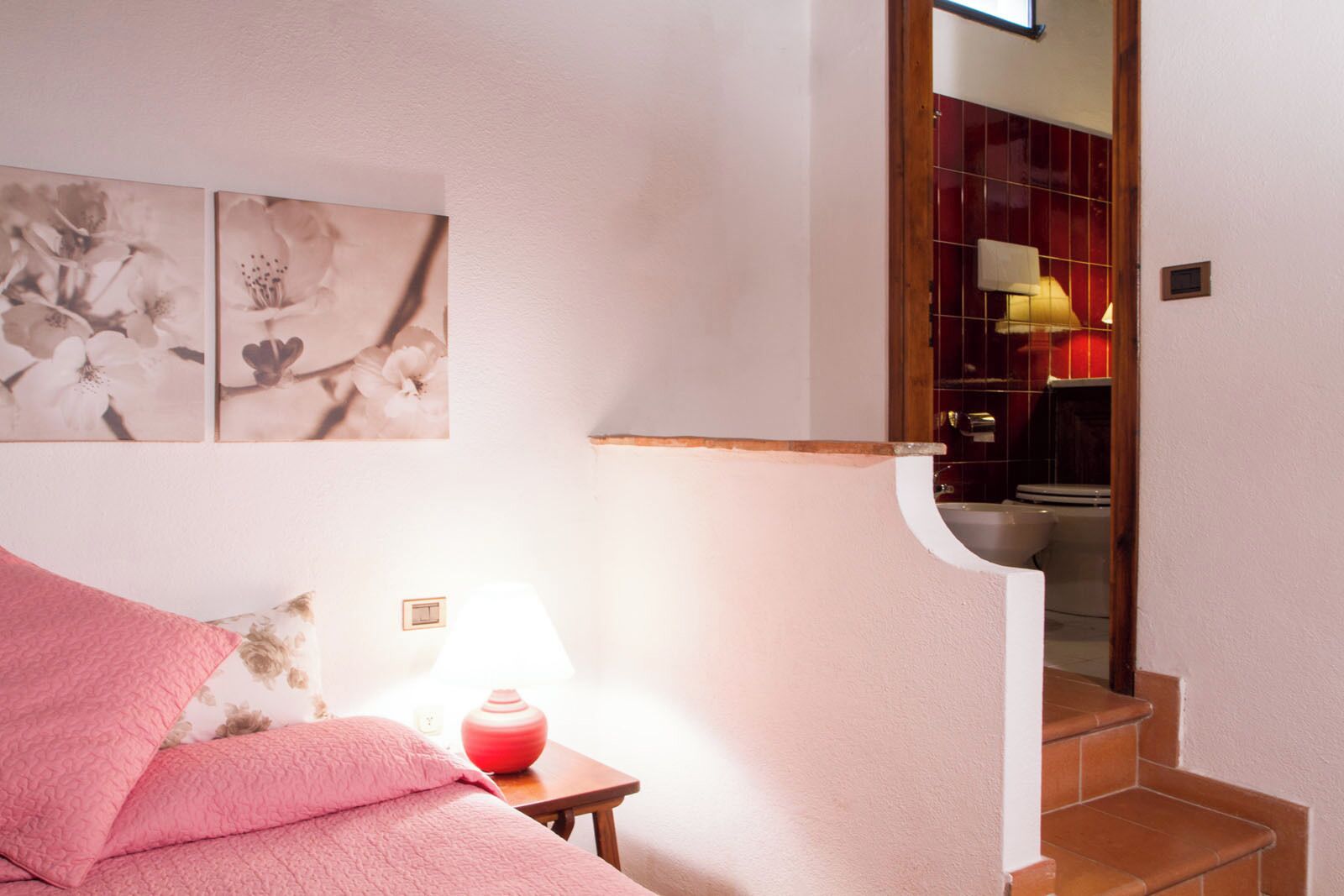 Quarto com uma cama, mesa de cabeceira com abajur e parede com duas obras de arte florais emolduradas.