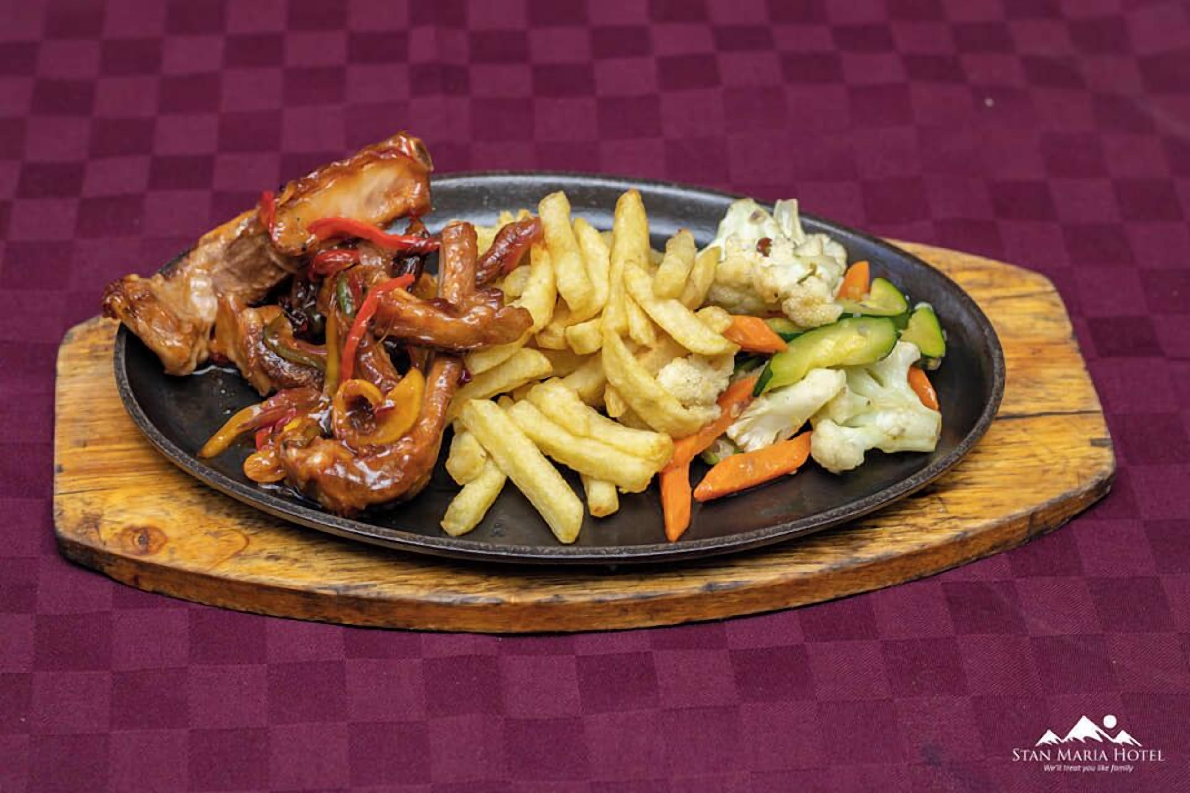 Prato de comida com carne, batatas fritas e legumes em uma tábua de madeira.