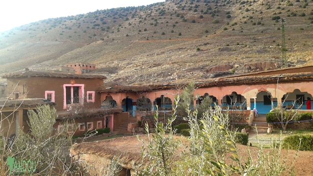 Um edifício tradicional com várias arcos e um telhado de palha, cercado por vegetação rasteira e uma paisagem montanhosa.