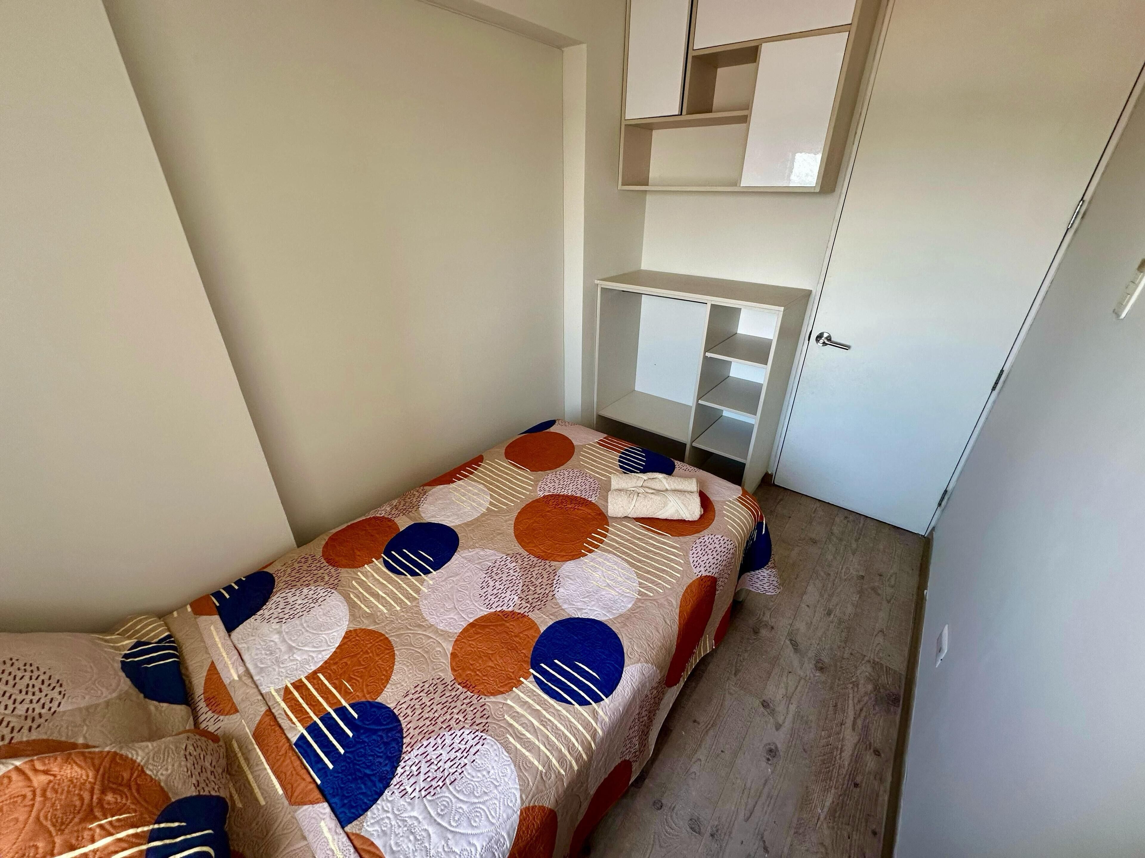 Um quarto pequeno e compacto, com uma cama, um guarda-roupa branco e uma escrivaninha embutida.