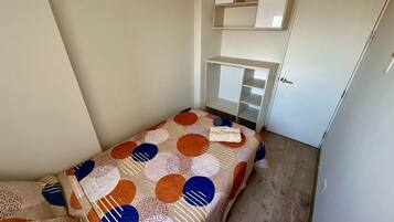 Um quarto pequeno e compacto, com uma cama, um guarda-roupa branco e uma escrivaninha embutida.