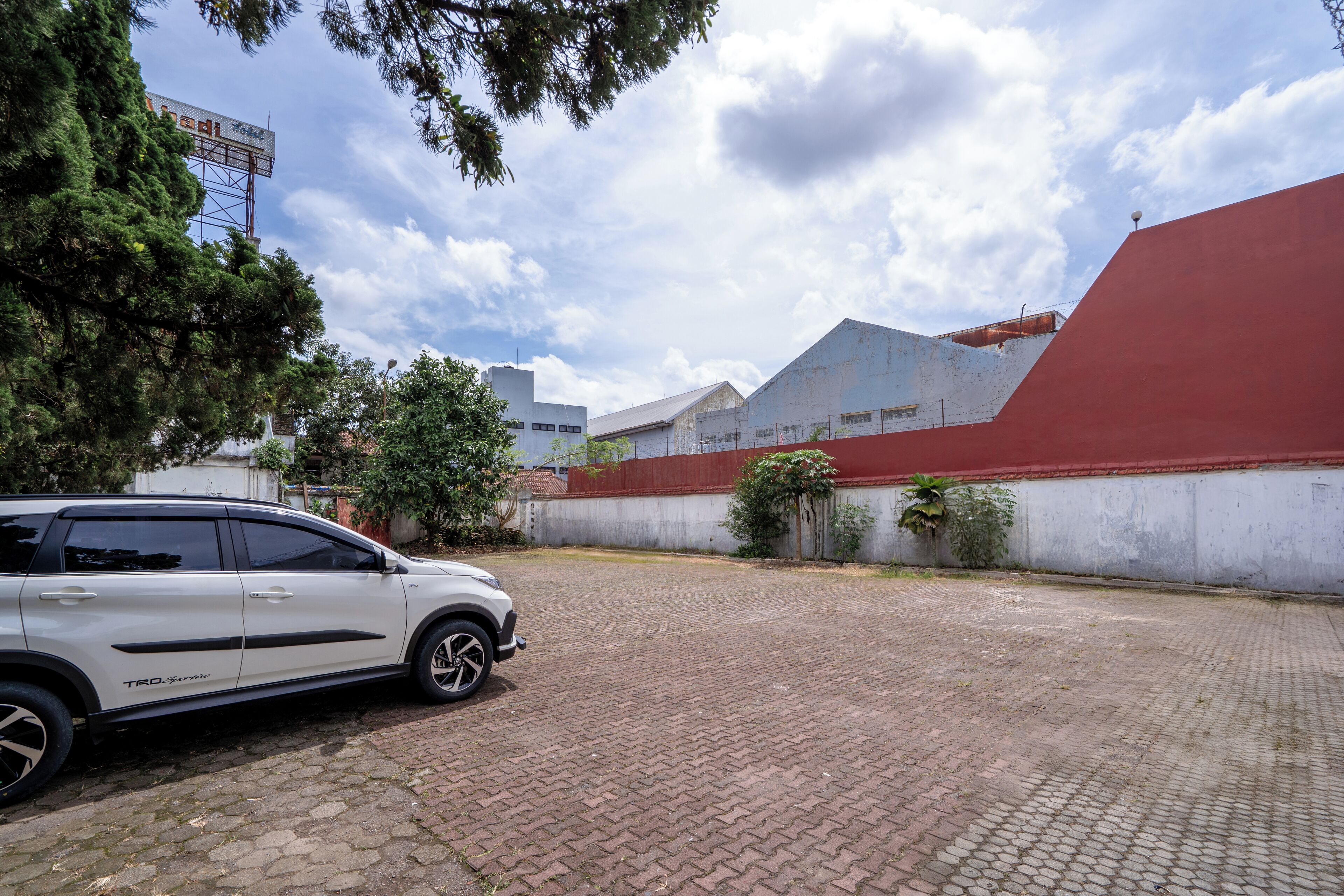 Um SUV branco estacionado em área pavimentada, com um prédio vermelho ao fundo.