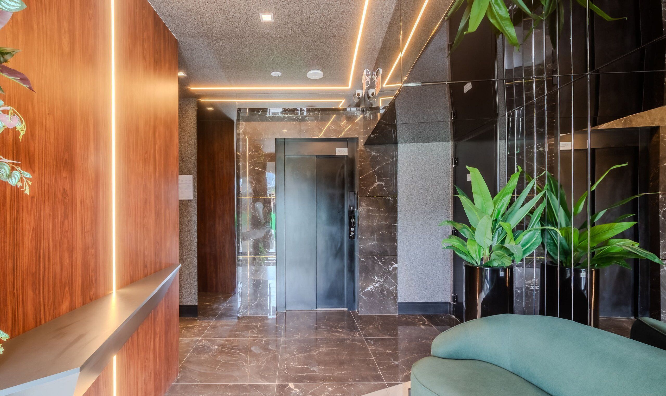 Um hall moderno com balcão de recepção, piso de mármore e um sofá verde.