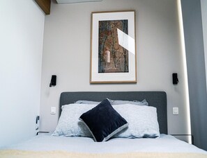 Uma cama com cabeceira cinza, duas almofadas e uma obra de arte emoldurada na parede acima.