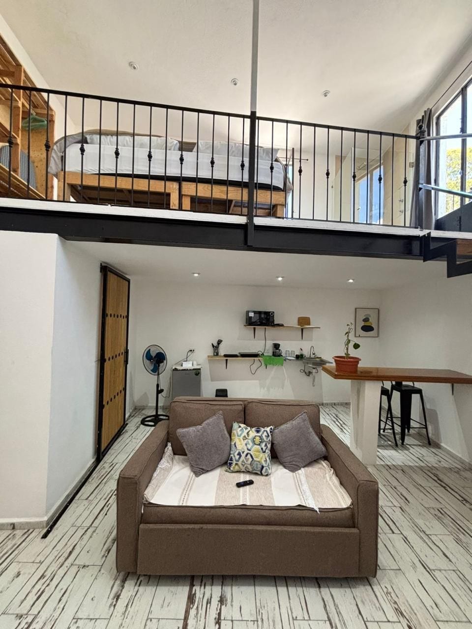 Um espaço de estar moderno estilo loft, com pé direito alto, sofá, área de jantar e cozinha.