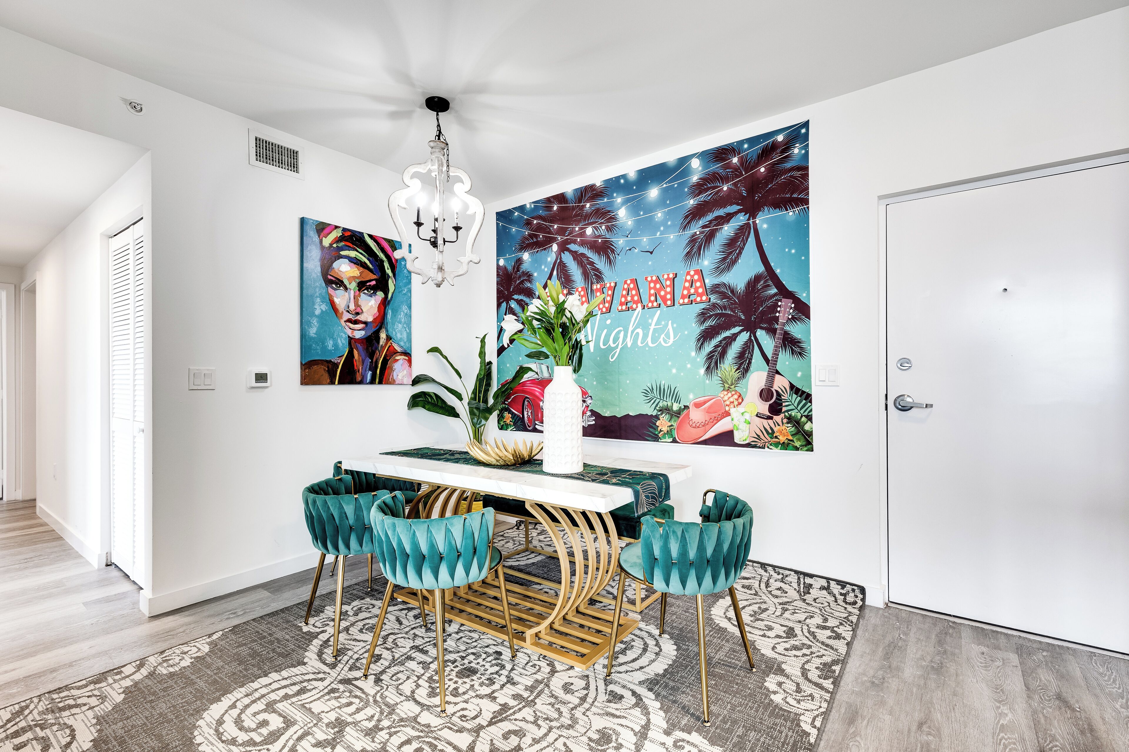 Uma área de jantar com uma mesa branca, cadeiras verde-água e um grande mural na parede.