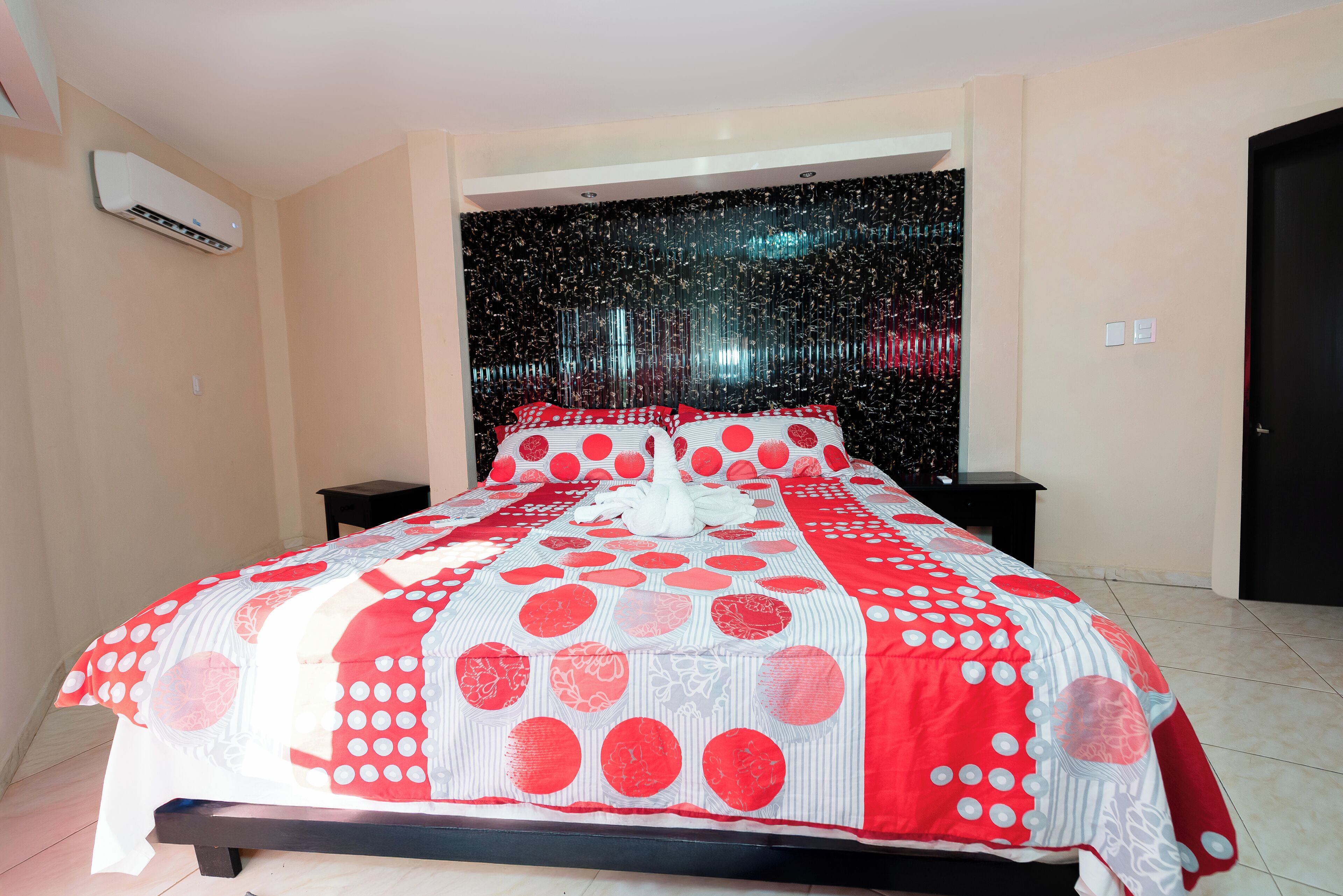 Quarto com cama coberta por um edredom listrado em vermelho e branco, travesseiro de cisne branco e cabeceira preta com vista para uma noite estrelada.
