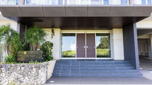 A modern building entrance with a stone wall, a sign reading "Grand Blue," and a staircase leading to a balcony.