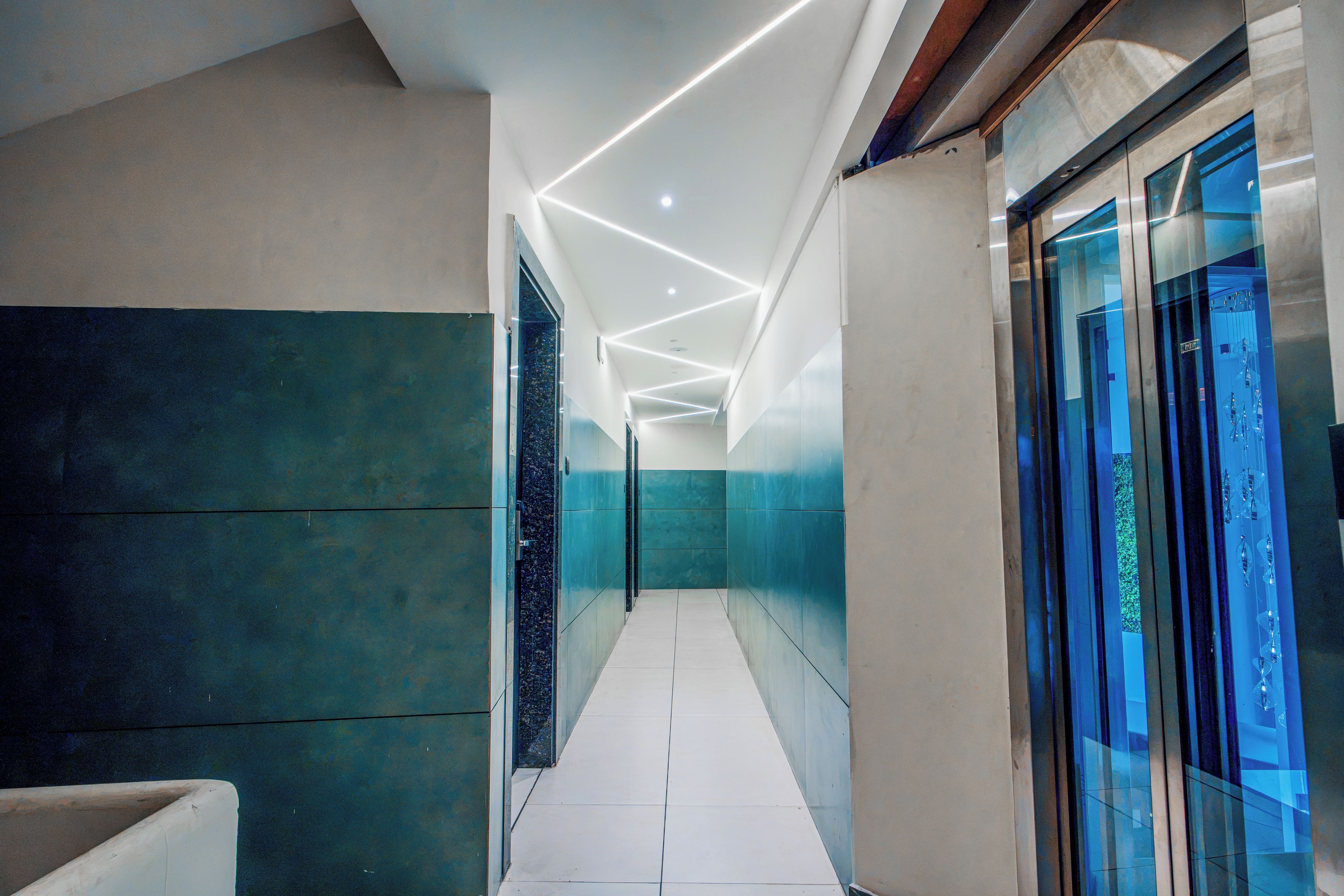 Um corredor moderno com design geométrico no teto, um elevador de vidro e piso revestido de azulejos.
