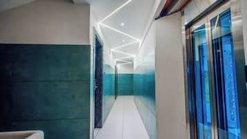 Um corredor moderno com design geométrico no teto, um elevador de vidro e piso revestido de azulejos.