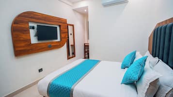 Quarto com cama, televisão fixada em painel de madeira, ar condicionado na parede e porta que dá para outro cômodo.