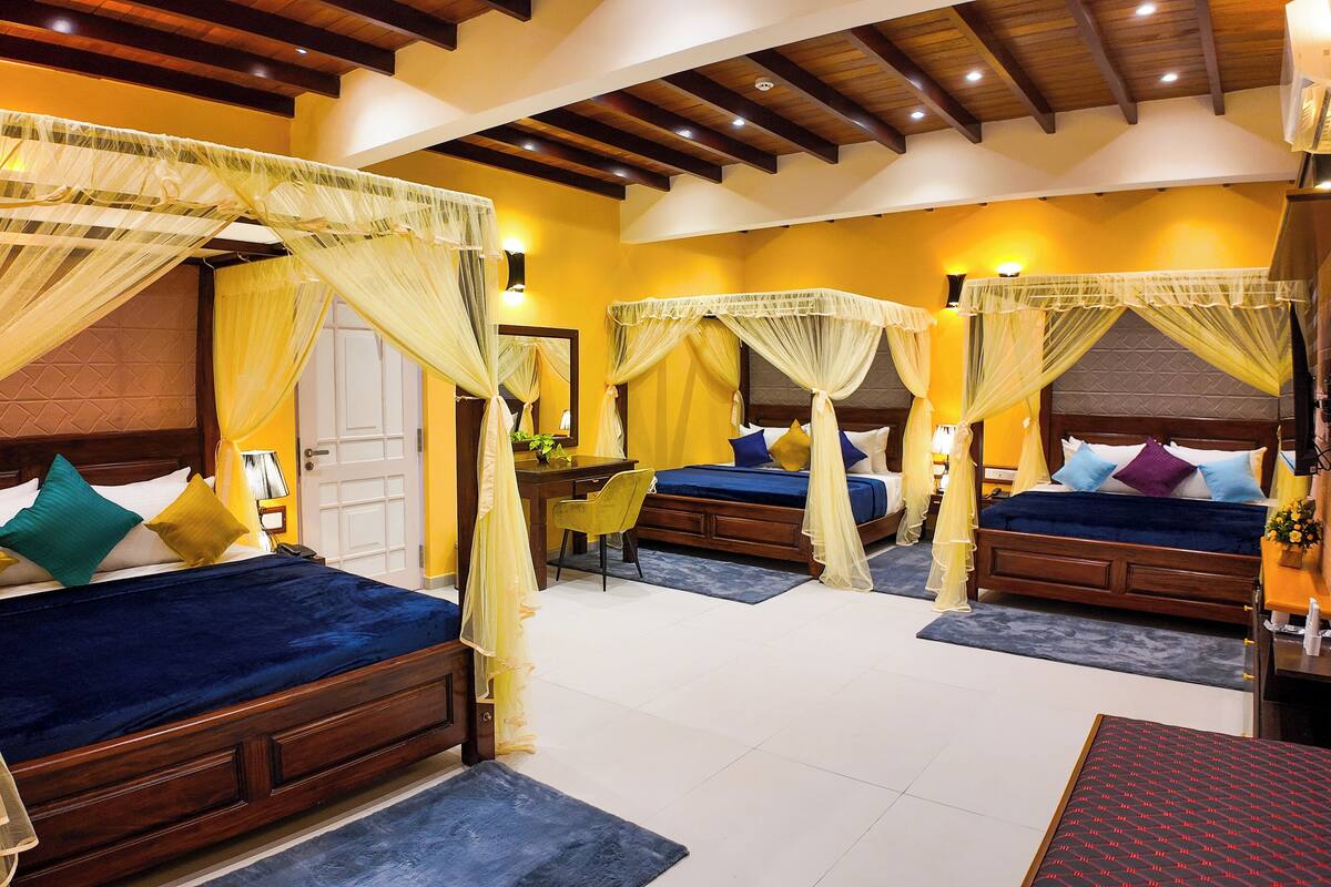 Quarto de hotel com quatro camas, cada uma com dossel e roupa de cama de cores diferentes.