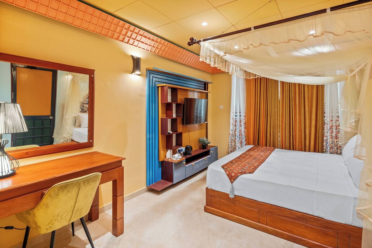 Quarto de hotel com cama, escrivaninha, cadeira, televisão e espelho.