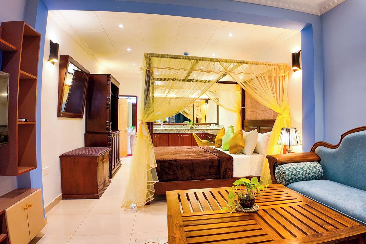 Quarto de hotel com cama, sofá, mesa de centro de madeira e banheiro visível por uma porta.