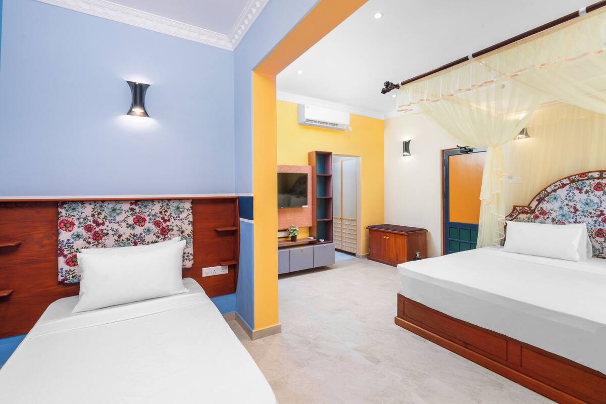 Quarto de hotel com duas camas, um guarda-roupa, uma mesa de toucador e uma janela com cortina.