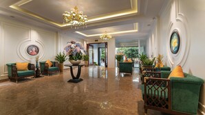 Um hall amplo com sofás estofados em tons de verde, um arranjo floral central e um candelabro.