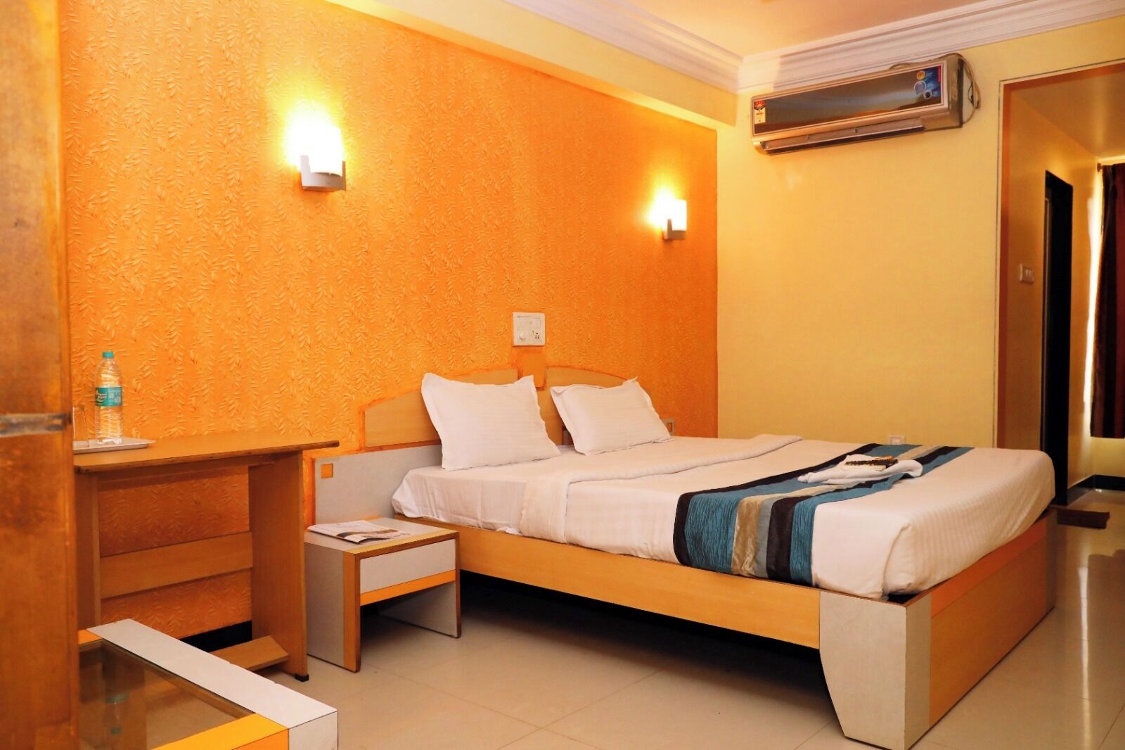 Quarto de hotel com cama, mesa de cabeceira, luminária e aparelho de ar condicionado.