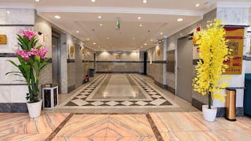 Um hall de hotel com piso de mármore, balcão de recepção e plantas em vasos.