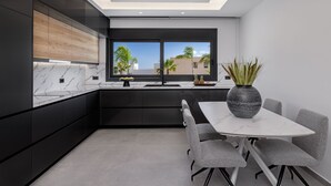 Uma cozinha moderna com armários escuros, painel de parede em mármore e uma grande janela com vista para palmeiras e edifícios.