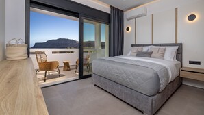 Quarto moderno com uma cama grande, mesa de cabeceira de madeira, cadeira de vime e vista para uma paisagem montanhosa através de uma porta de vidro deslizante.