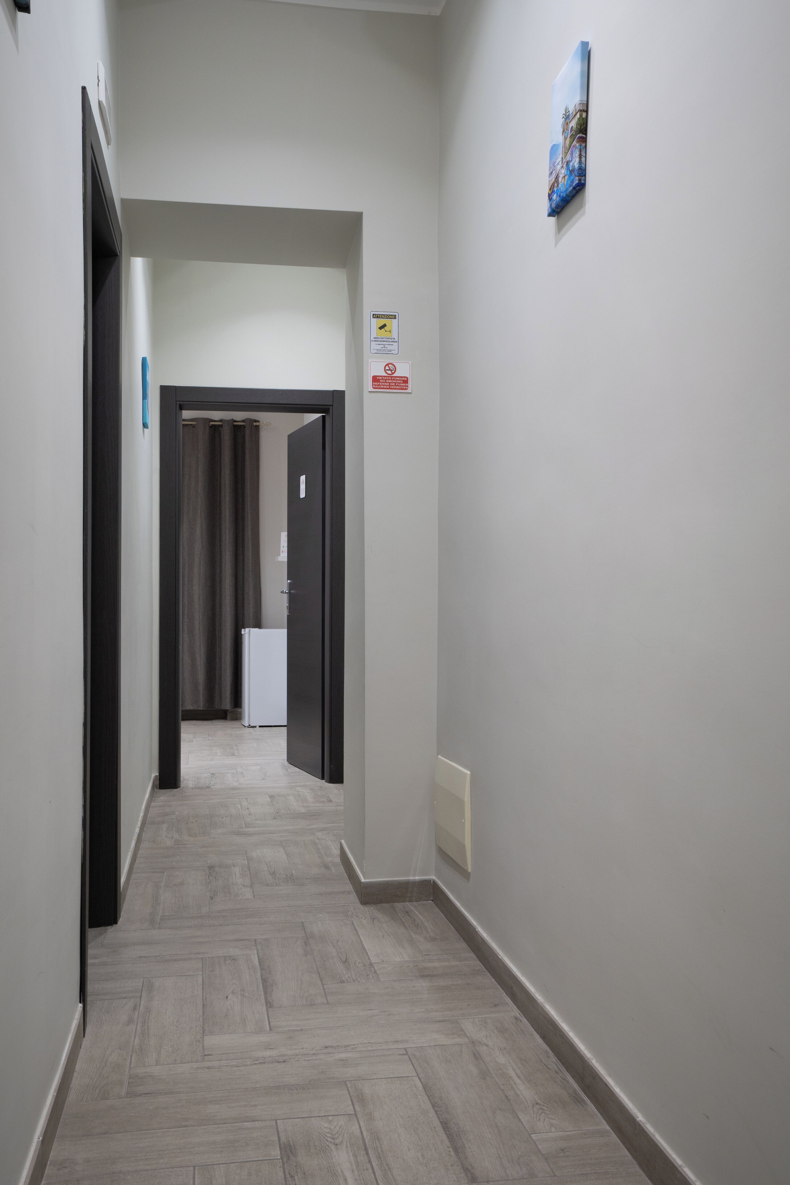 Um corredor com piso em padrão herringbone, uma porta no final e um quadro na parede.