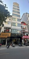 Um edifício de vários andares com um hotel elegante no andar térreo, uma fachada visível com uma placa, e um prédio escolar à direita.
