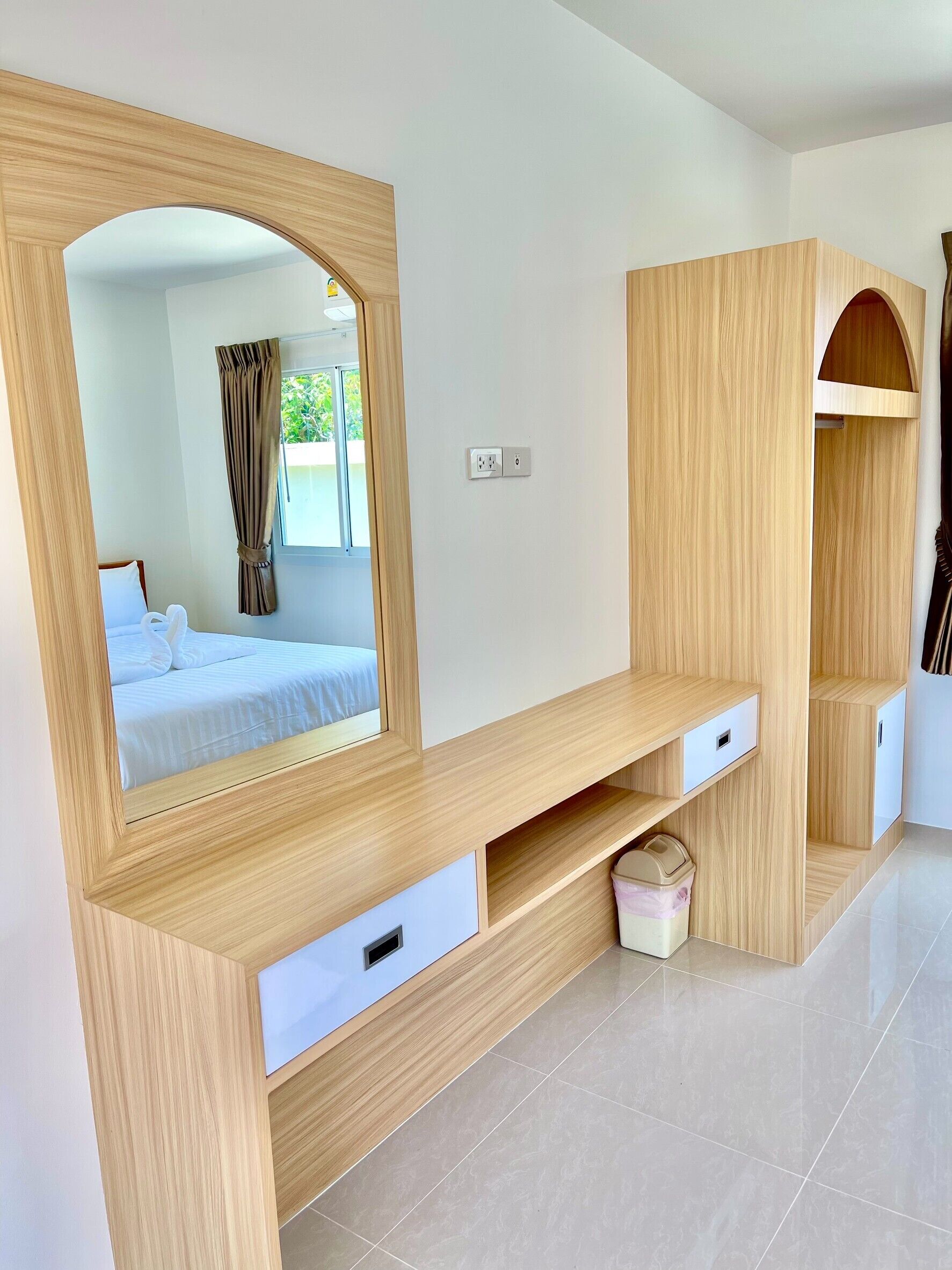 Quarto moderno com toucador de madeira, um espelho grande e uma cama com roupa de cama branca.