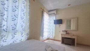 Quarto de hotel com cama, mesa de cabeceira com espelho, televisão e janela com cortinas.