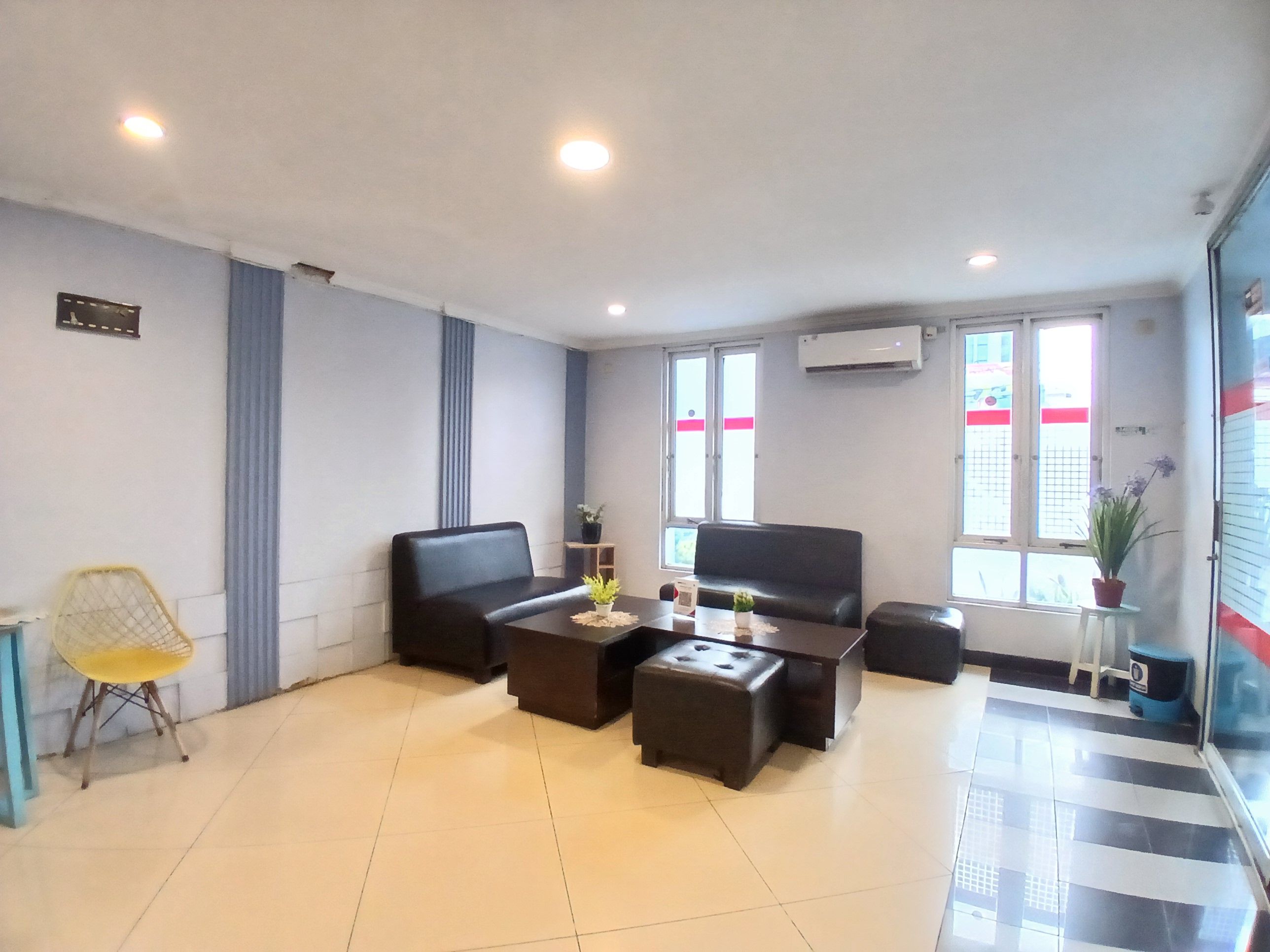 Uma sala de estar moderna com um sofá, dois pufes, uma mesa de centro e uma mesinha lateral com uma planta.
