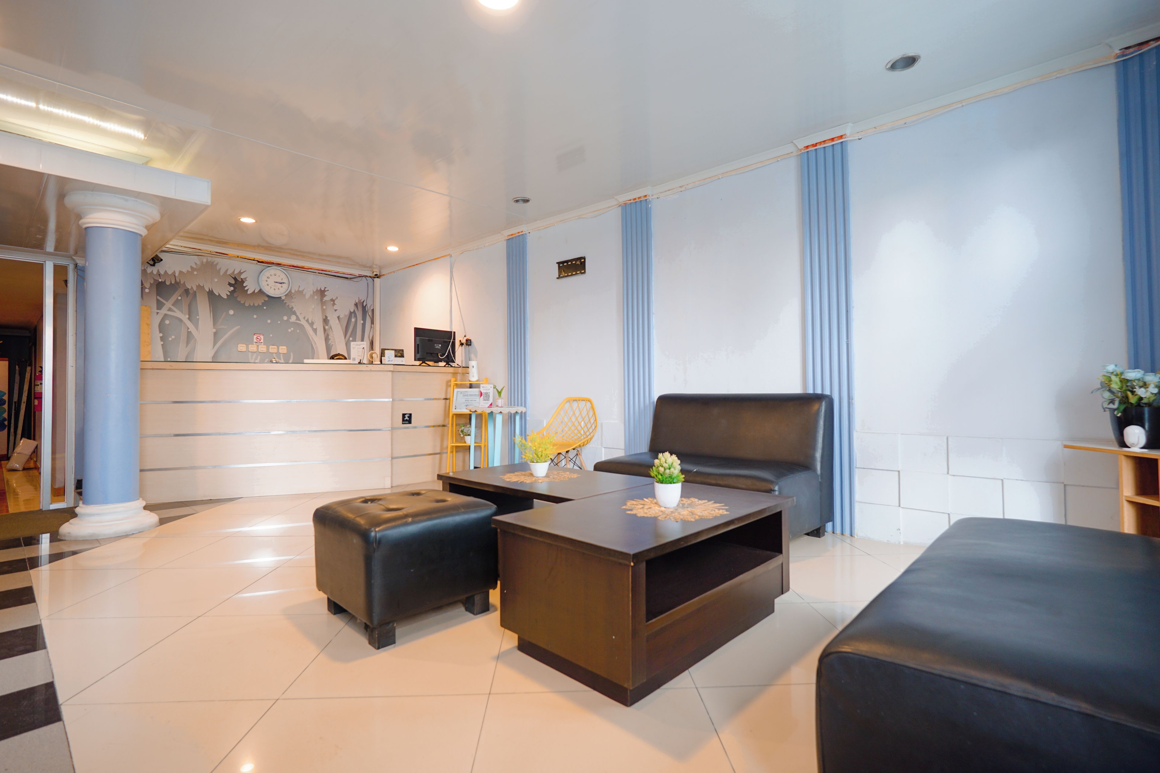 Um lobby de hotel moderno com uma mesa de recepção, um sofá de couro preto, uma mesa de centro e uma pequena planta.