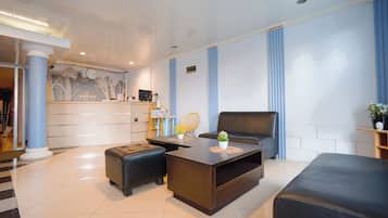 Um lobby de hotel moderno com uma mesa de recepção, um sofá de couro preto, uma mesa de centro e uma pequena planta.
