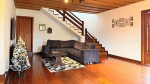Uma sala de estar espaçosa com teto de madeira, escada, sofá, mesa de centro e árvore de Natal.