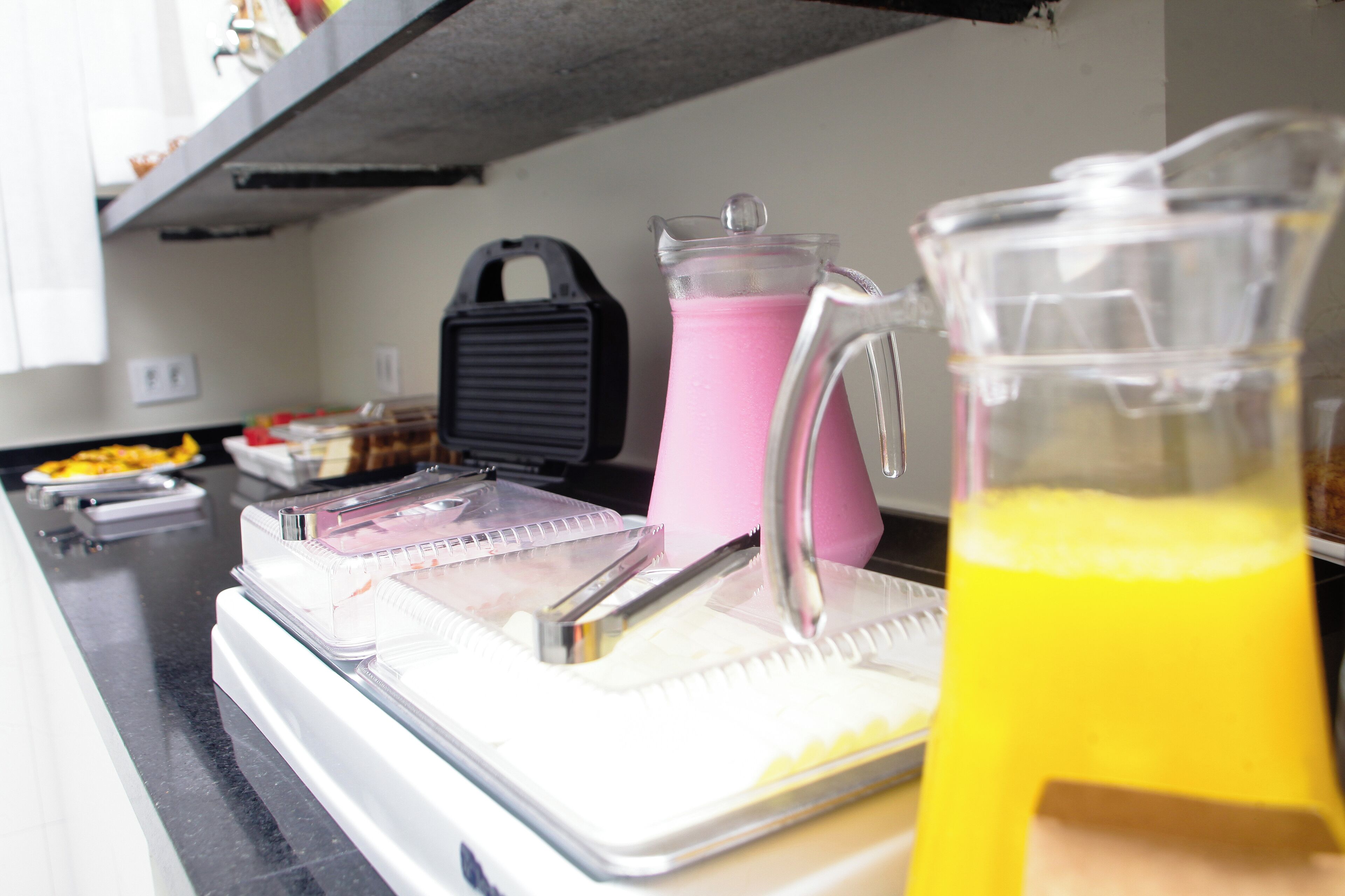 Uma mesa de buffet com diversos recipientes de comida e um jarro de suco de laranja.