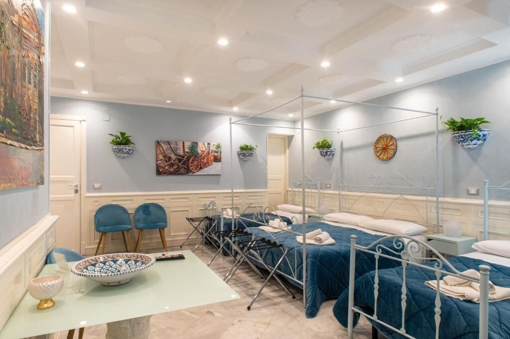 Quarto de hotel com uma cama grande, uma mesa pequena, duas cadeiras, uma planta fixada na parede e um ventilador de teto.