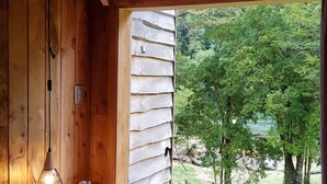 Quarto de cabana de madeira com cama, lumin ária pendente e janela com vista para o verde.