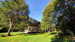 Um edifício de madeira tradicional com telhado inclinado, rodeado por árvores verdes exuberantes e um céu azul límpido.