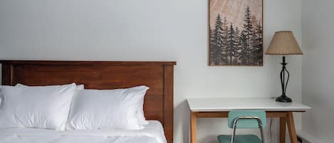 Quarto de hotel com cama, escrivaninha, cadeira, abajur e pintura da parede com tema de floresta.