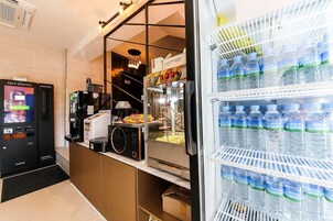 Espaço de autoatendimento com baralho de cartas, máquina de pipoca e frigorífico abastecido com garrafas de água.